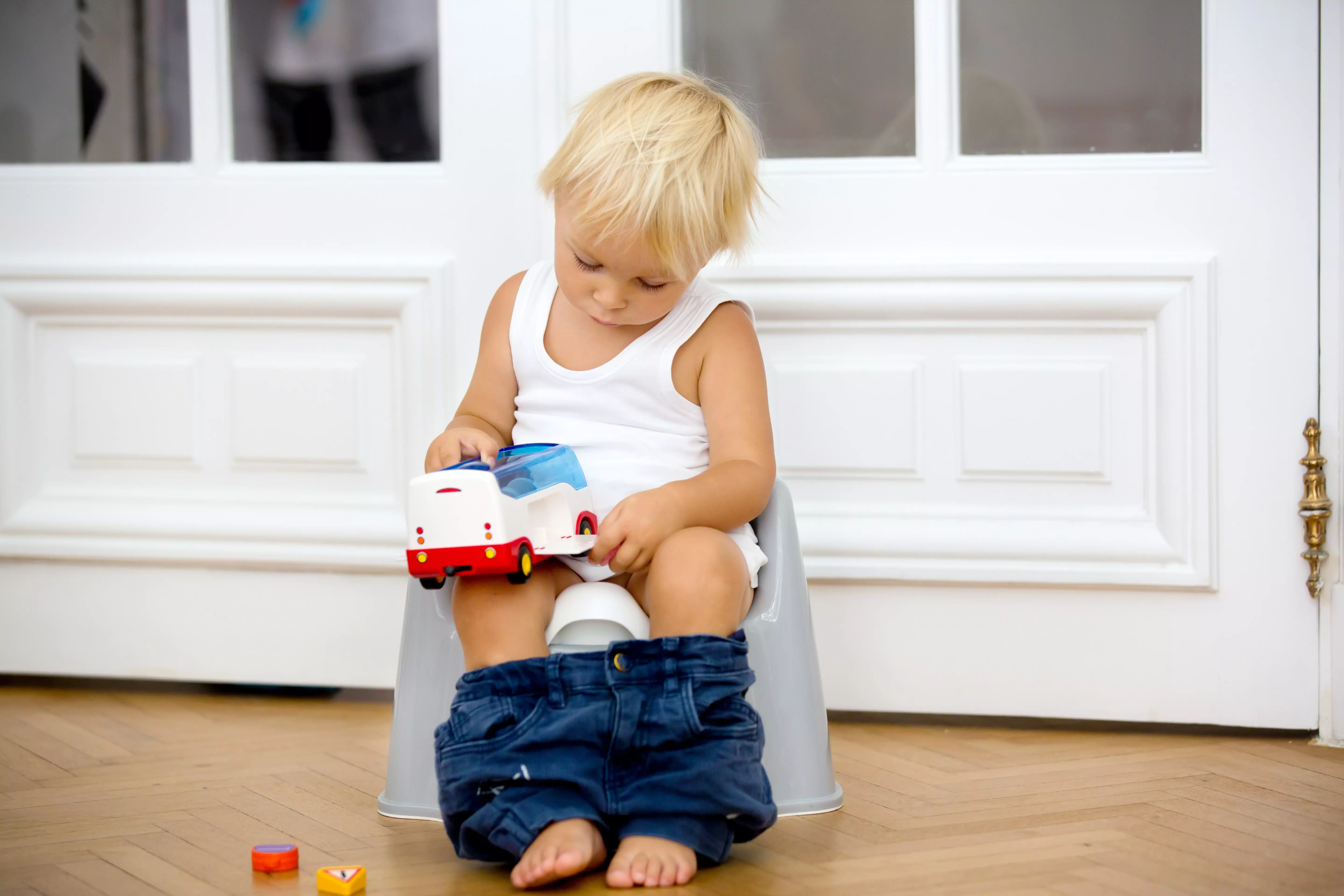 Bayi anak bayi laki-laki balita duduk di toilet, bermain dengan mainan di ruang tamu, di dalam ruangan