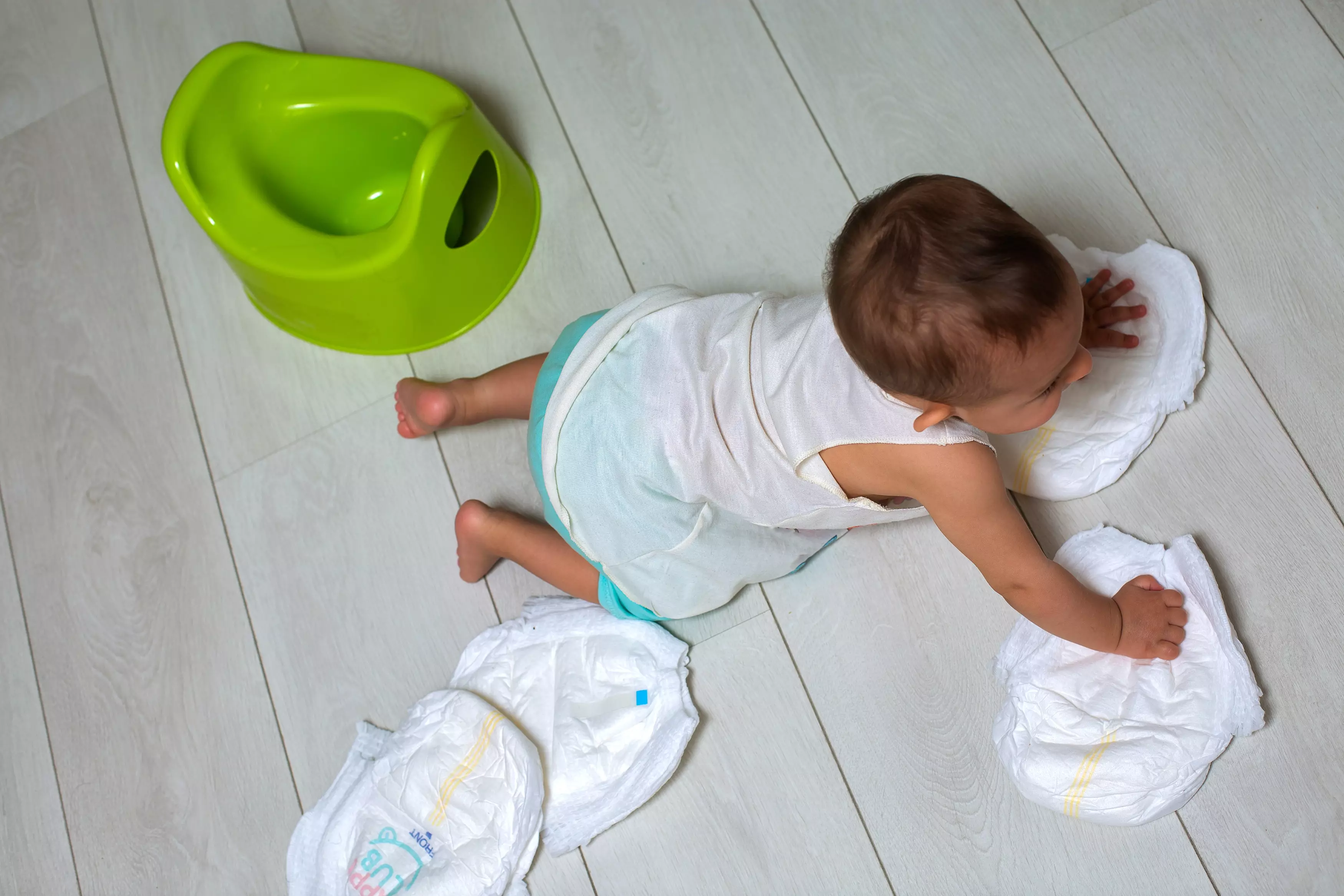 konsep pelatihan toilet. Seorang bayi kecil yang lucu di sebuah kamar di lantai yang terang bermain dengan popok dan ...