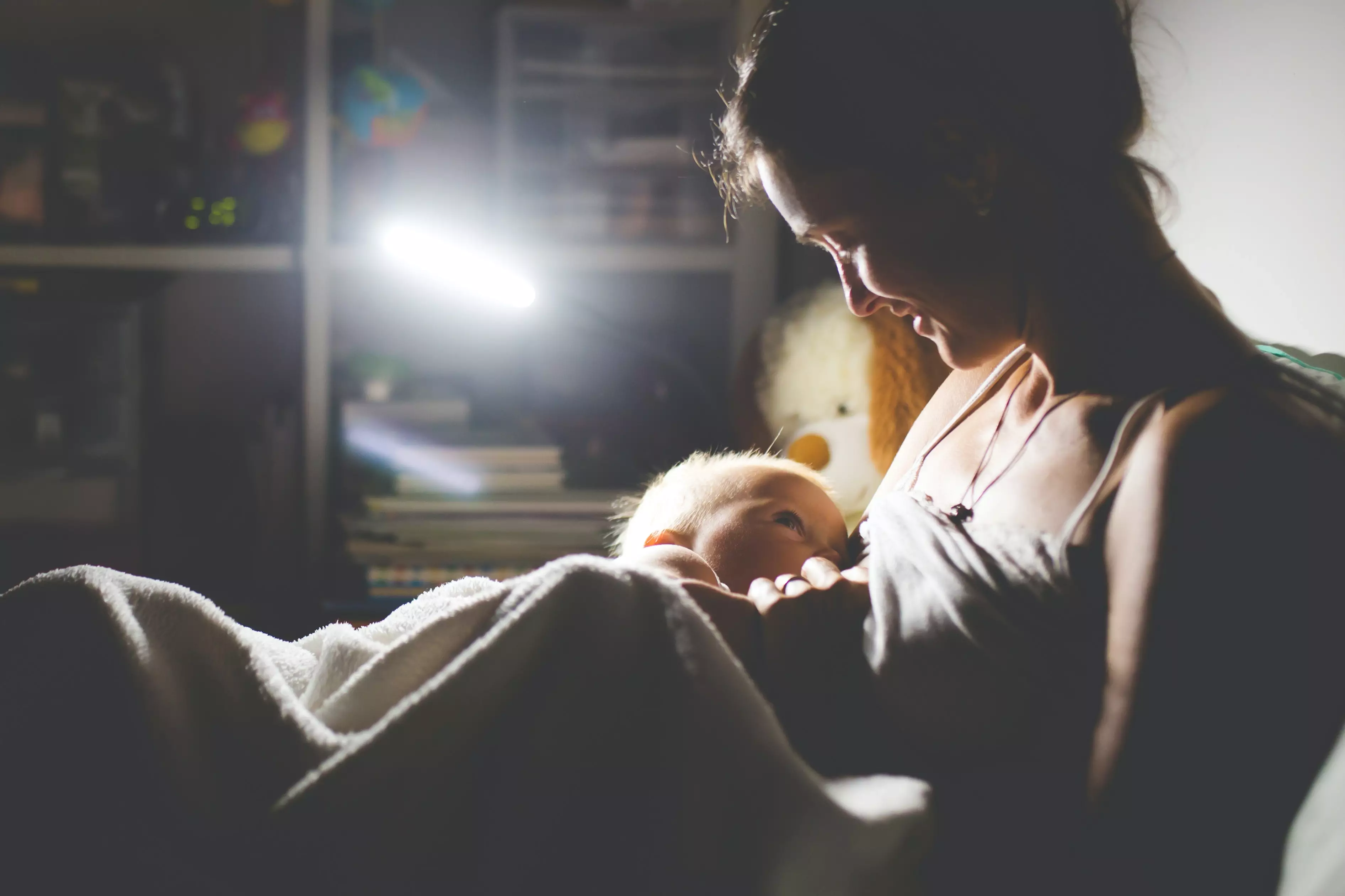 Ung falleg móðir, með nýfædda drenginn sinn á brjósti á kvöldin, dauft ljós. Mamma með barn á brjósti í...