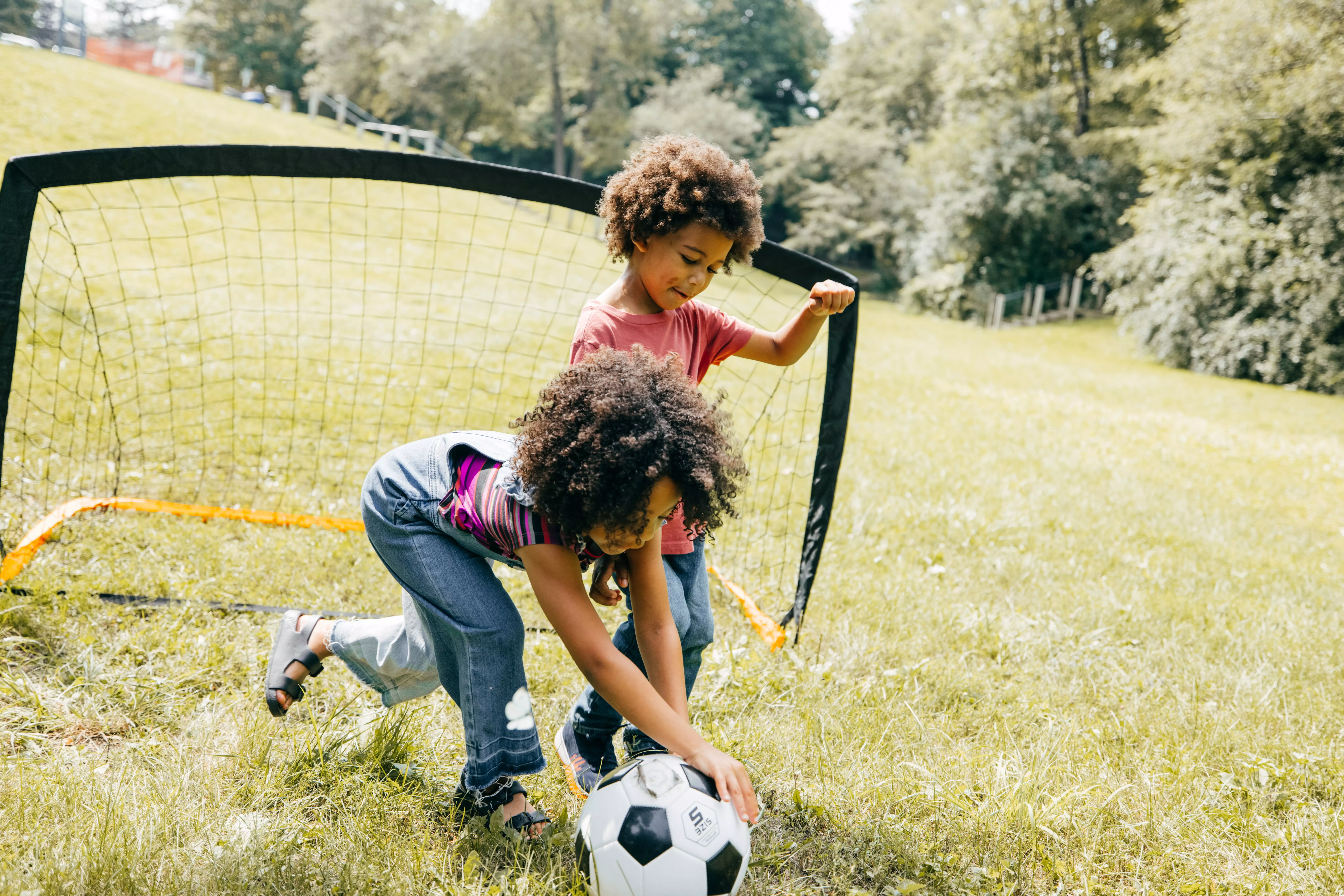 Záber na deti základných rokov, ktoré spolu hrajú futbal v školskom poli počas prestávky.