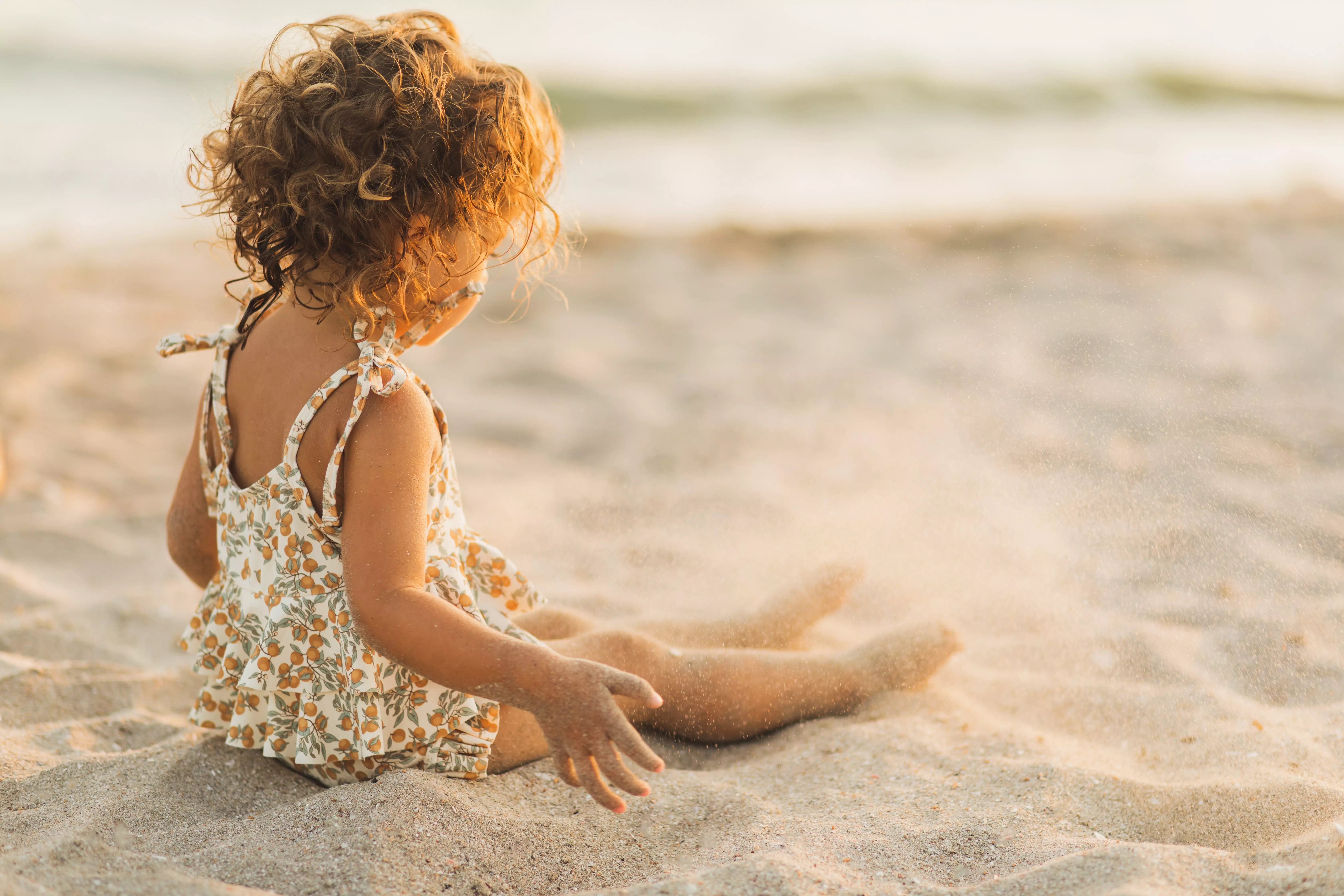 Glad latter liten jente som leker med sand på vakker tropisk strand under aktiv sommerfamilie...